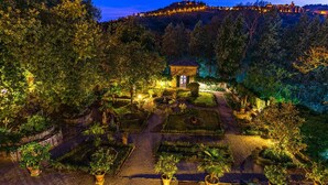 Um jardim bem iluminado com uma estrutura central, rodeado por diversas plantas e caminhos.