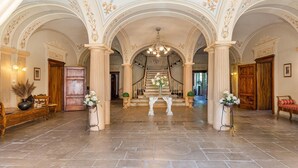 Um hall imponente com uma escadaria de mármore, colunas ornamentadas e um candelabro.