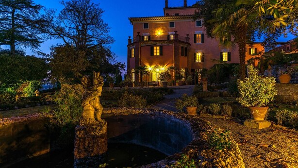 Um edifício com vários andares, uma entrada bem iluminada e um jardim com um pequeno lago.
