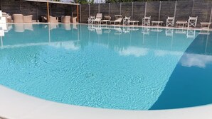 Piscina límpida com espreguiçadeiras e uma cerca de madeira ao fundo.