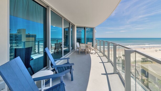 Varanda com vista para a praia, equipada com cadeiras e uma mesa.
