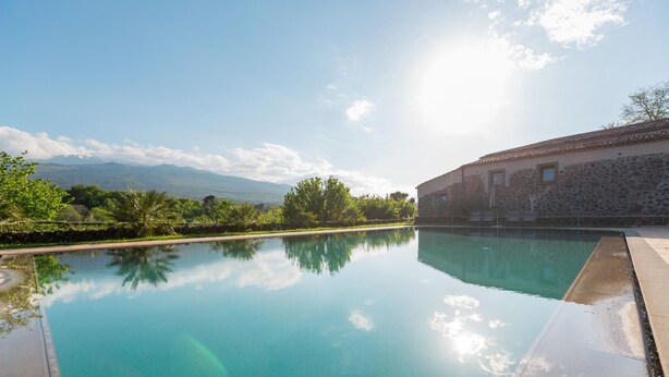 Piscina cristalina com parede de pedra e vista para montanhas ao fundo.