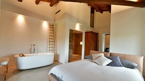 Quarto com uma cama grande, uma banheira e uma escada de madeira.