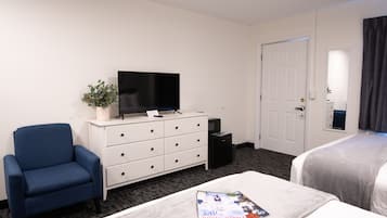 Quarto de hotel com duas camas, uma televisão sobre uma cômoda, uma cadeira e uma pequena planta.