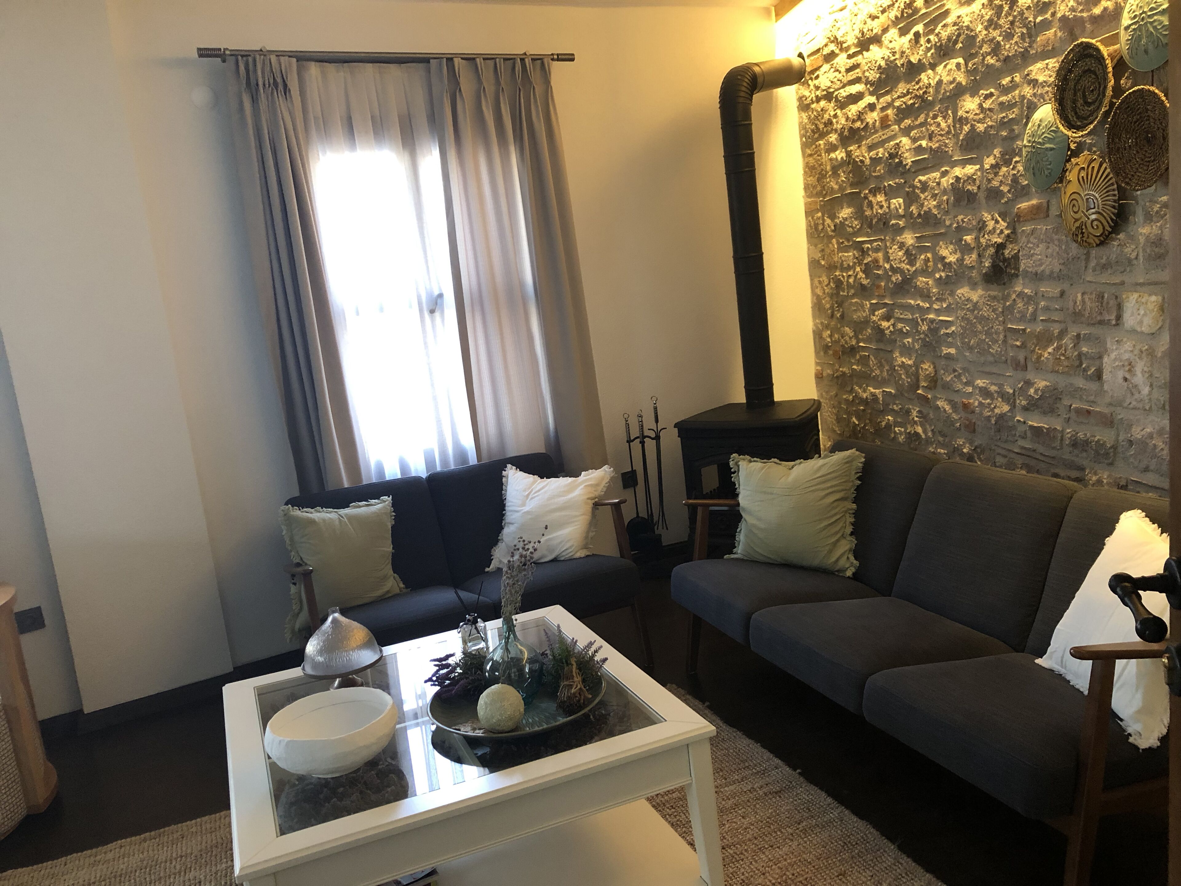 Uma sala de estar aconchegante com parede de pedra, lareira, sofá e mesa de centro com objetos decorativos.