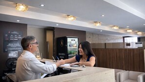 Uma receção com um homem e uma mulher a conversar, um frigorífico e um quadro de ementa fixado na parede.