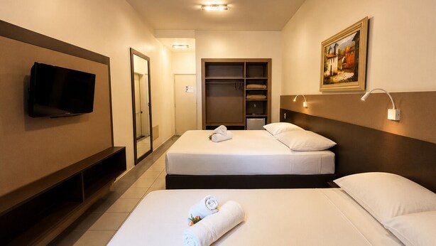 Quarto de hotel com duas camas, televisão, guarda-roupa, um quadro e abajur.