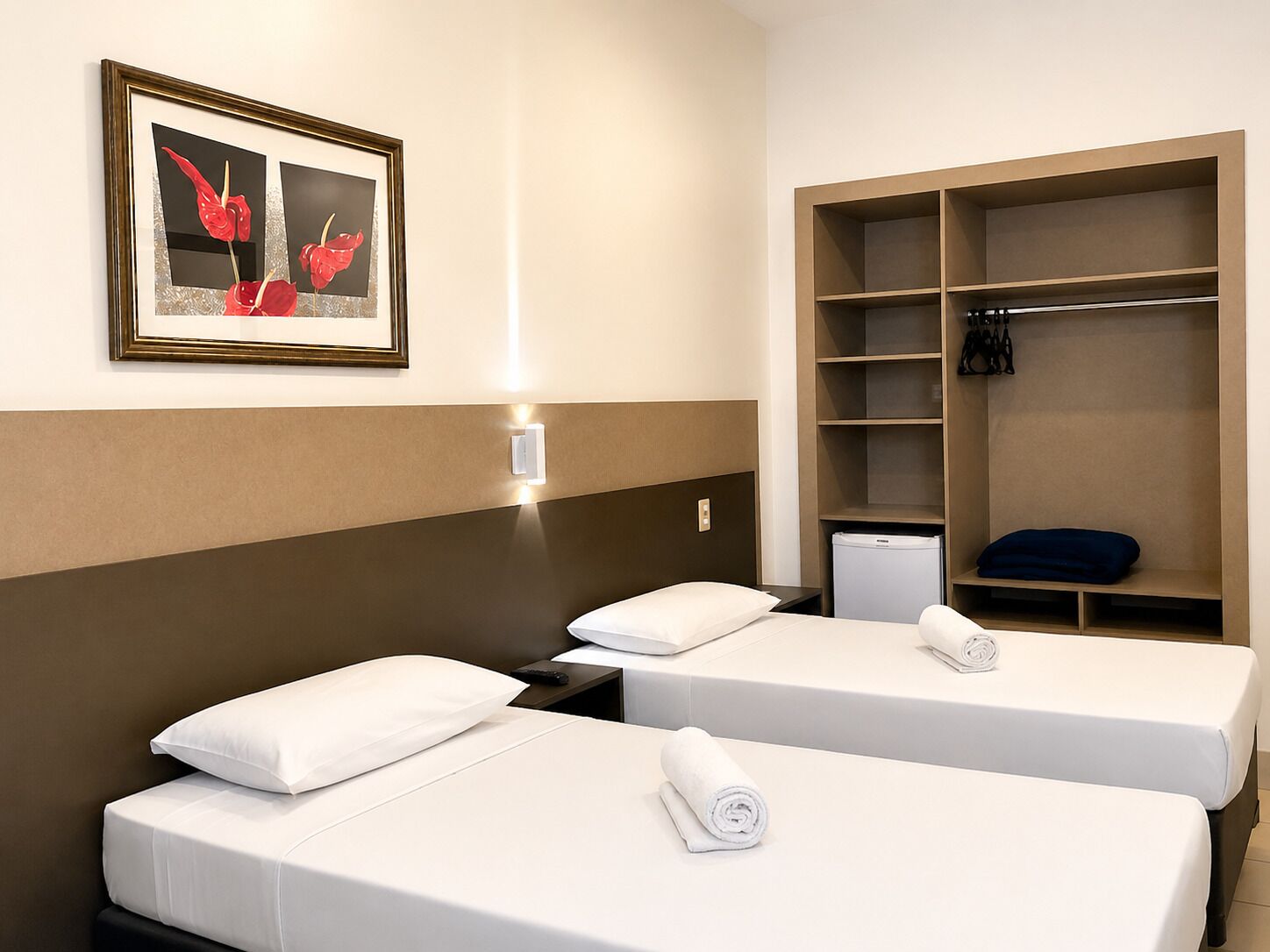 Quarto de hotel com duas camas, um guarda-roupa, um quadro emoldurado e um pequeno frigorífico.