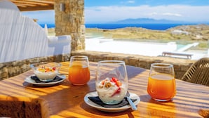 Uma mesa com sobremesa, um copo de suco de laranja e um copo de líquido âmbar, emoldurada por uma vista panorâmica.