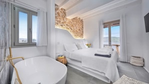 Quarto moderno com uma banheira grande, cama com toalhas bem dobradas e parede de destaque em pedra.