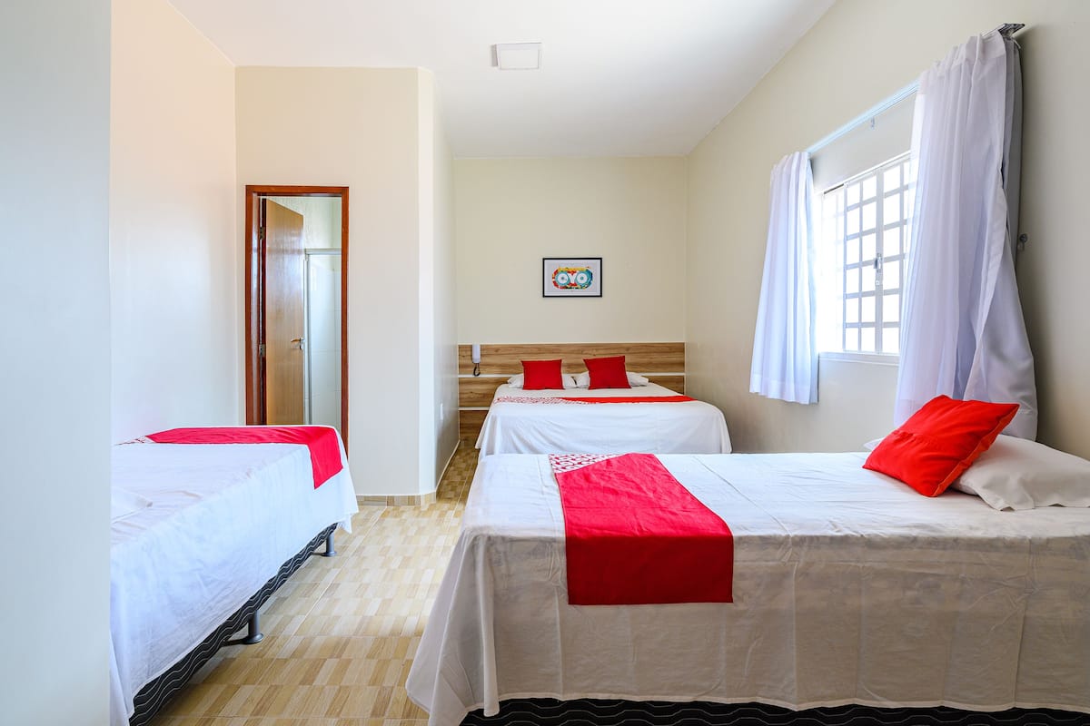 Quarto de hotel com duas camas, cabeceira de madeira, janela com cortinas e uma porta.