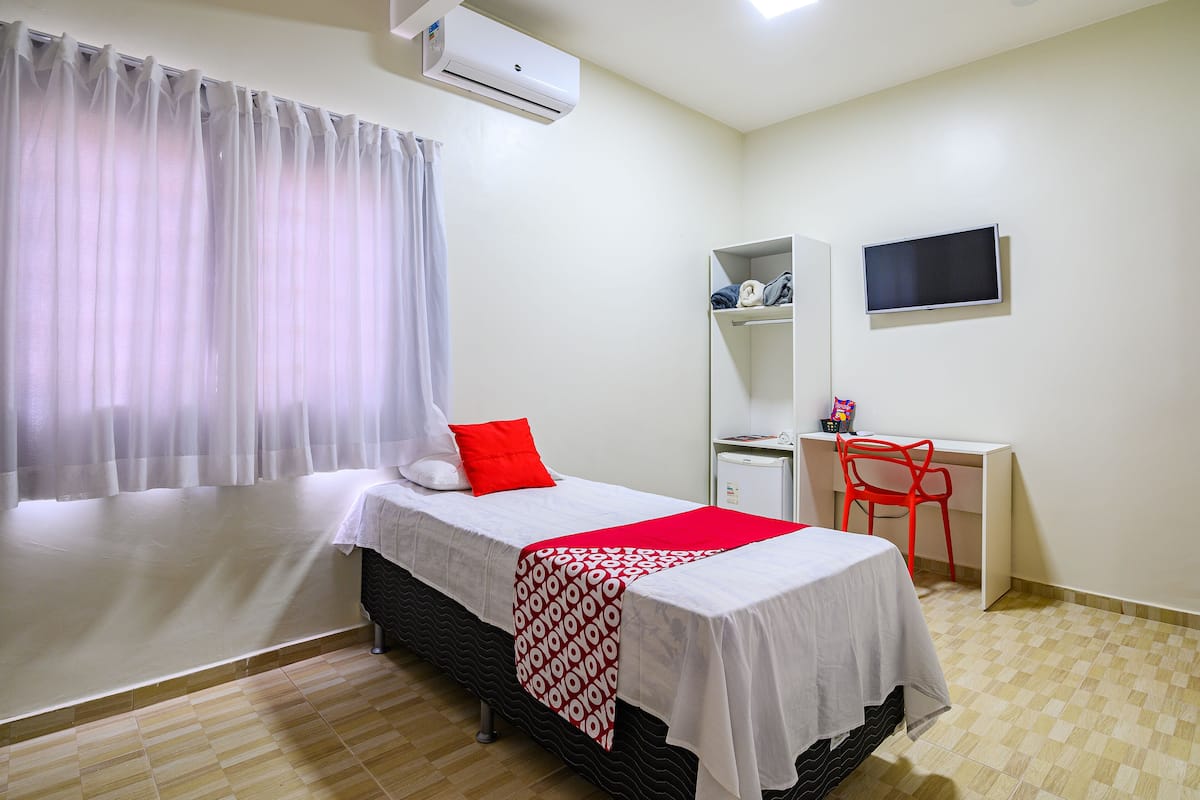 Quarto com cama, escrivaninha, cadeira, televisão e ar condicionado.