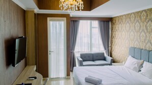 Quarto de hotel com cama, televisão, área de estar e um candelabro.