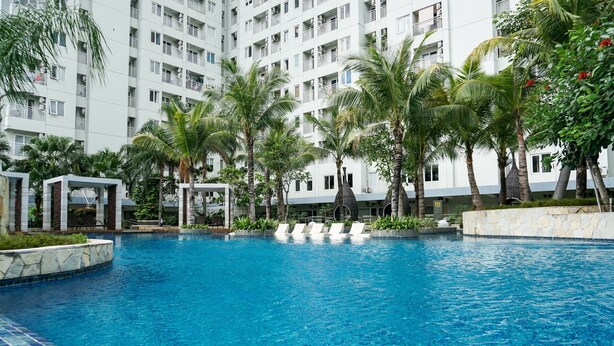 Uma piscina com água azul cristalina, rodeada por palmeiras e um edifício alto ao fundo.