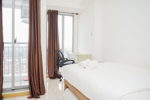 Quarto de hotel com cama, cadeira, escrivaninha e janela com cortinas.