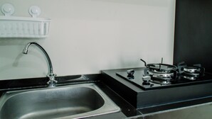 Cozinha com pia de aço inoxidável, fogão preto e parede branca.
