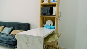 Uma sala de estar moderna com um sofá cinza escuro, uma mesa de centro de mármore branco e uma estante de madeira com micro-ondas e chaleira.