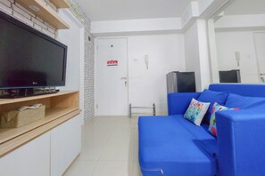 Uma sala de estar moderna com televisão de tela plana, um sofá azul e um pequeno armário.