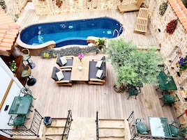 Uma área de piscina no terraço com deck de madeira, piscina, móveis de exterior e plantas em vasos.