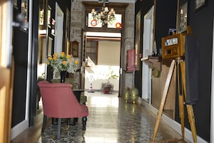 Um corredor com uma cadeira vermelha, um cavalete de madeira e um vaso com flores.