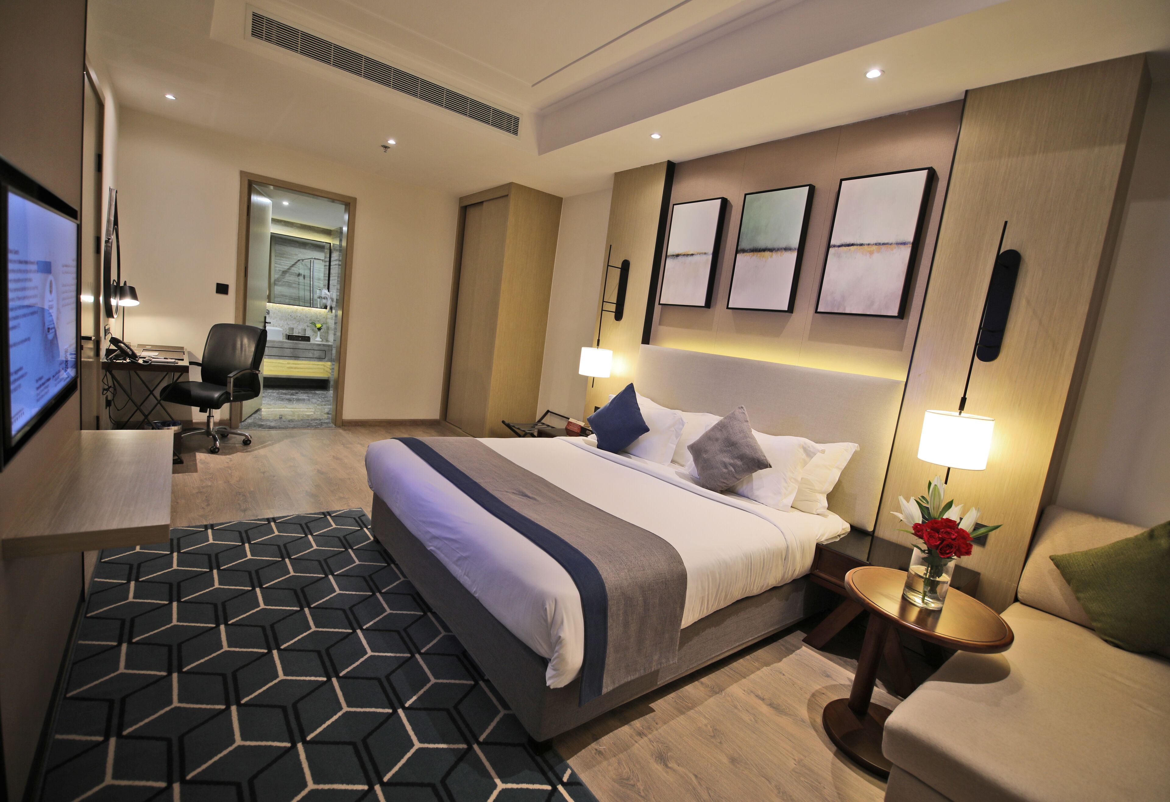 Quarto de hotel moderno com uma cama grande, mesas de cabeceira, escrivaninha e televisão.