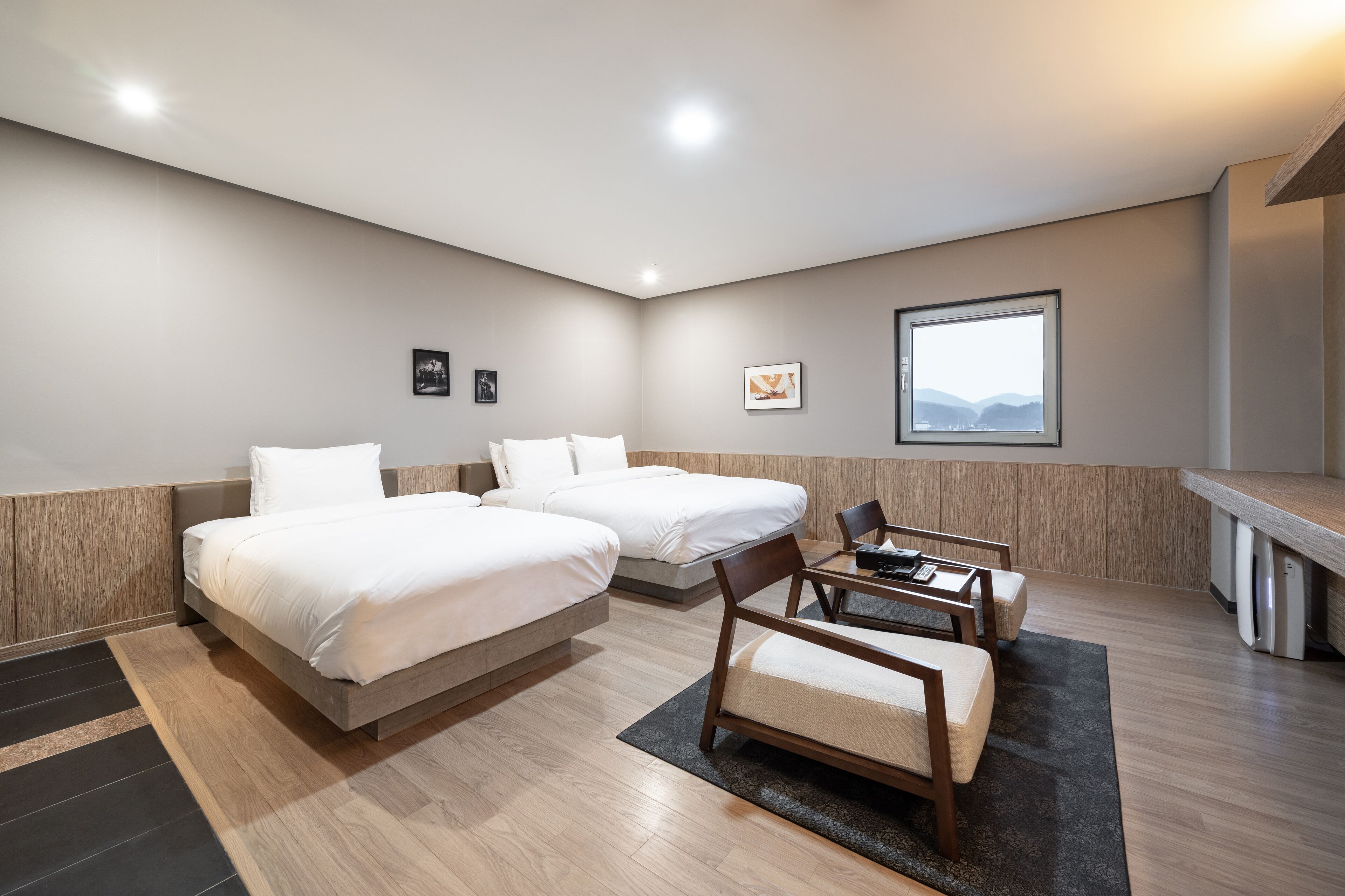 Quarto de hotel moderno com duas camas, uma escrivaninha e vista para as montanhas pela janela.