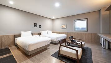 Quarto de hotel moderno com duas camas, uma escrivaninha e vista para as montanhas pela janela.