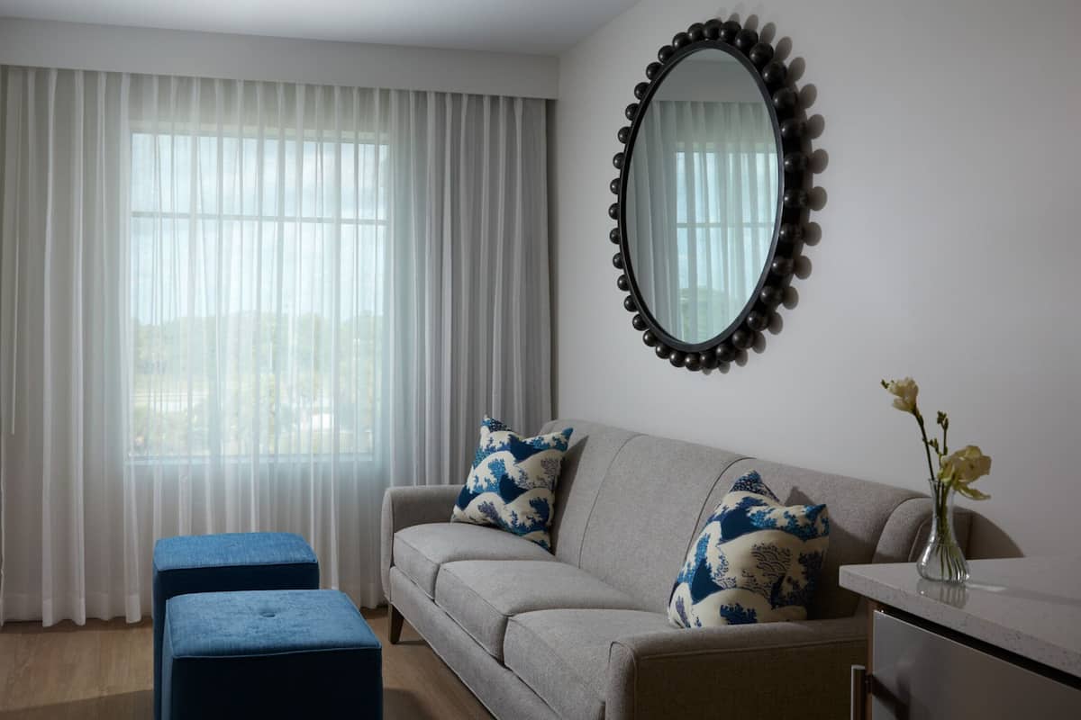 Uma sala de estar moderna com um sofá cinza, pufes azuis, um espelho grande e um vaso com flores.