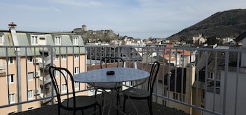 Varanda com mesa e cadeiras redondas, vista para paisagem urbana com edifícios e uma colina.