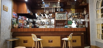 Uma área de bar com decoração em madeira, prateleiras cheias de garrafas e dois bancos.