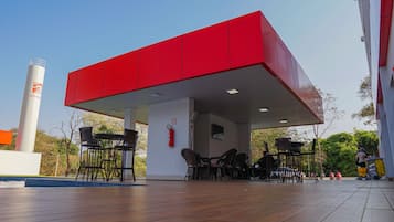 Um posto de gasolina com toldo vermelho, área de estar externa e extintor de incêndio.