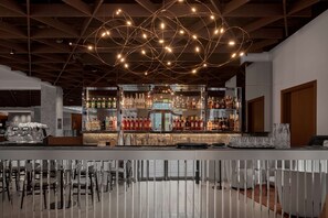 Espaço de bar com design moderno, apresentando um balcão extenso com banquetas, variedade de garrafas e uma luminária de teto singular.