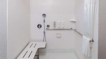 Área de duche com um banco, chuveiro manual e prateleira com artigos de higiene pessoal.