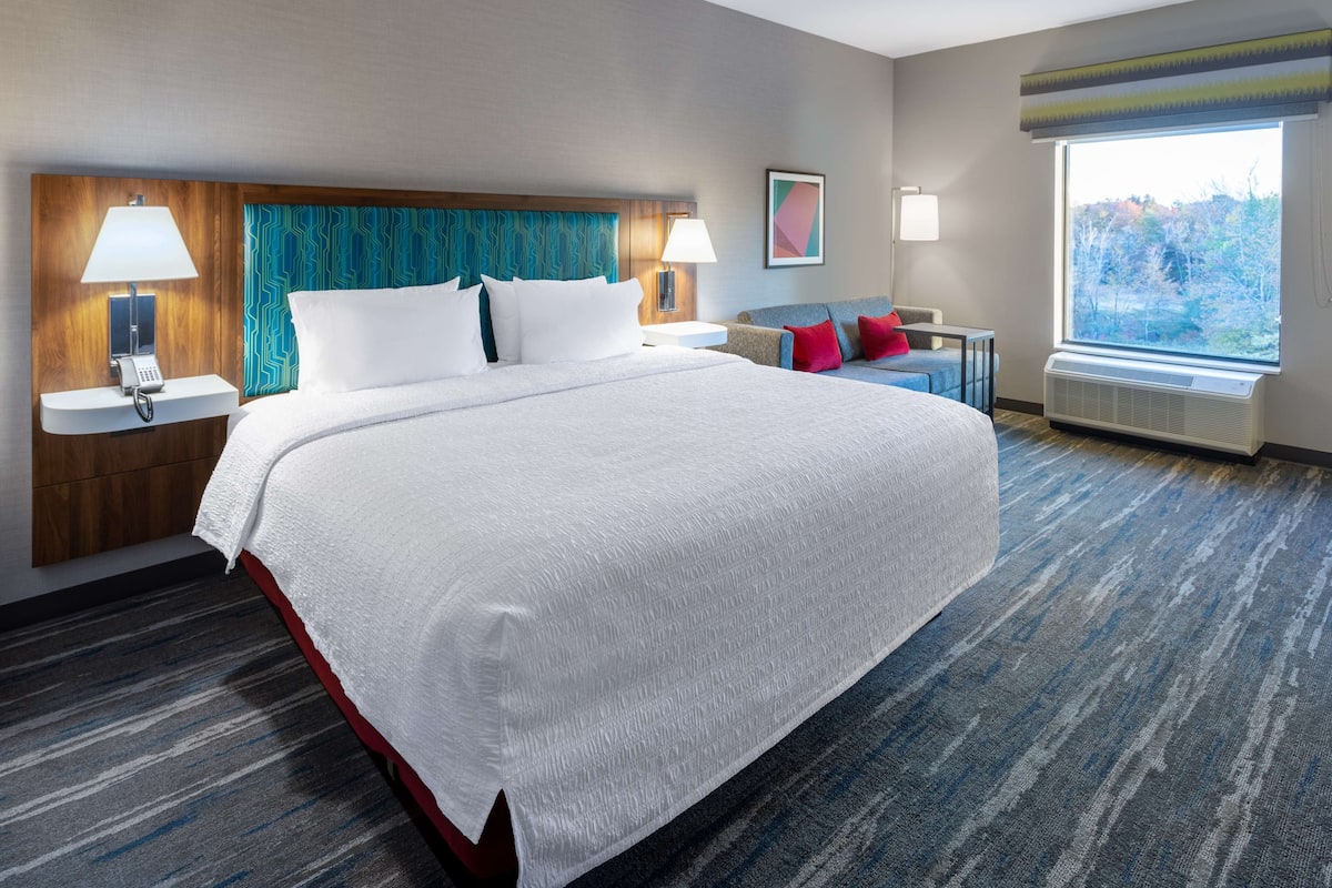 Quarto de hotel com uma cama grande, duas mesas de cabeceira com luminárias, uma janela com vista e cabeceira com padrão azul.
