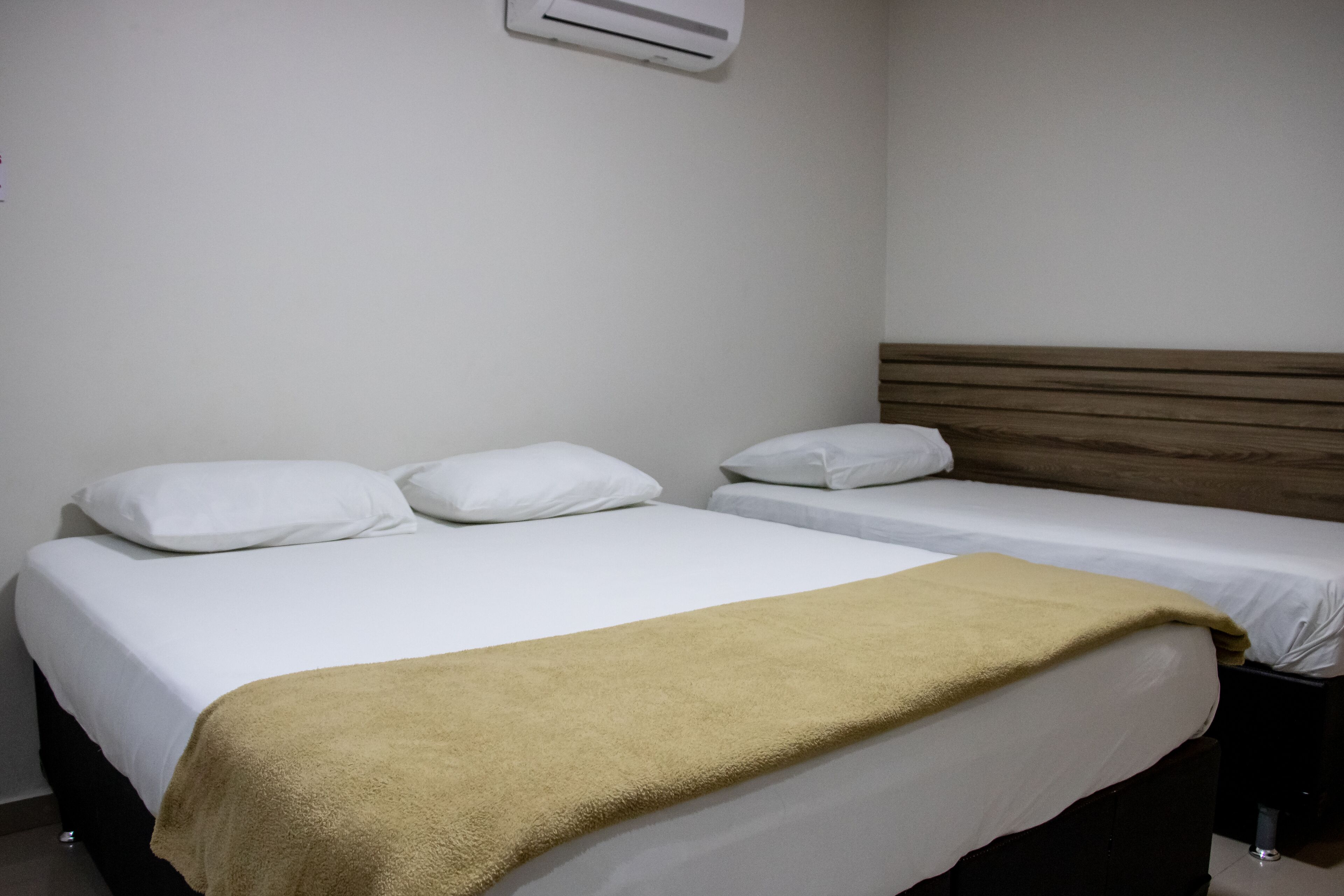 Quarto com duas camas de solteiro, cada uma com roupa de cama branca e cabeceira marrom.