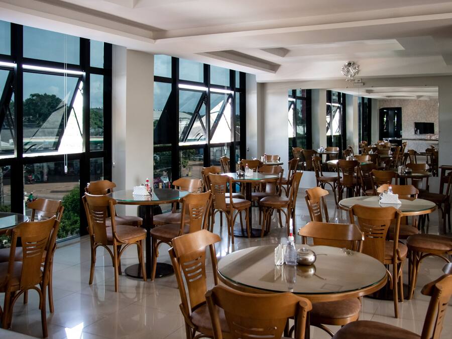 Um restaurante espaçoso com várias mesas e cadeiras, amplas janelas com vista para a paisagem urbana.