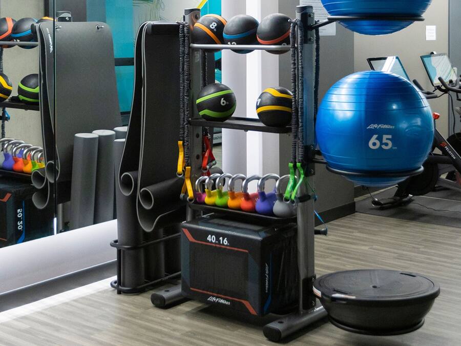 Uma academia com equipamentos de ginástica, incluindo um aparelho de musculação, bolas de medicina e uma bicicleta ergométrica.