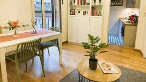 Uma área de refeições com mesa, cadeiras, um vaso de flores e uma estante repleta de livros e objetos decorativos.