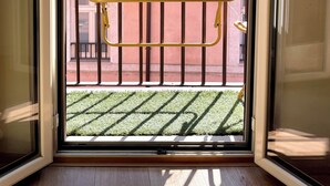 Uma varanda com guarda-corrimão de metal, uma mesa de madeira e um arranjo de flores.