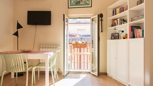 Quarto com mesa de jantar, cadeiras, estante, televisão e varanda com vista.