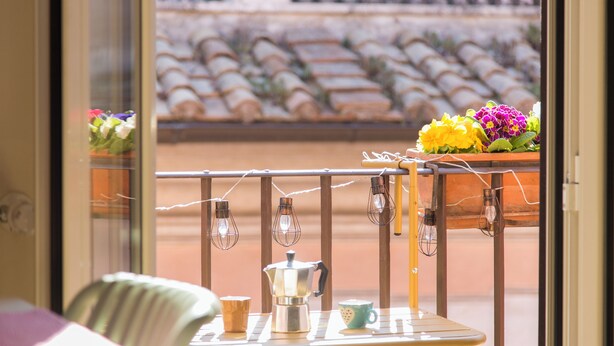 Uma varanda com mesa, cadeiras, cafeteira e lâmpadas penduradas.