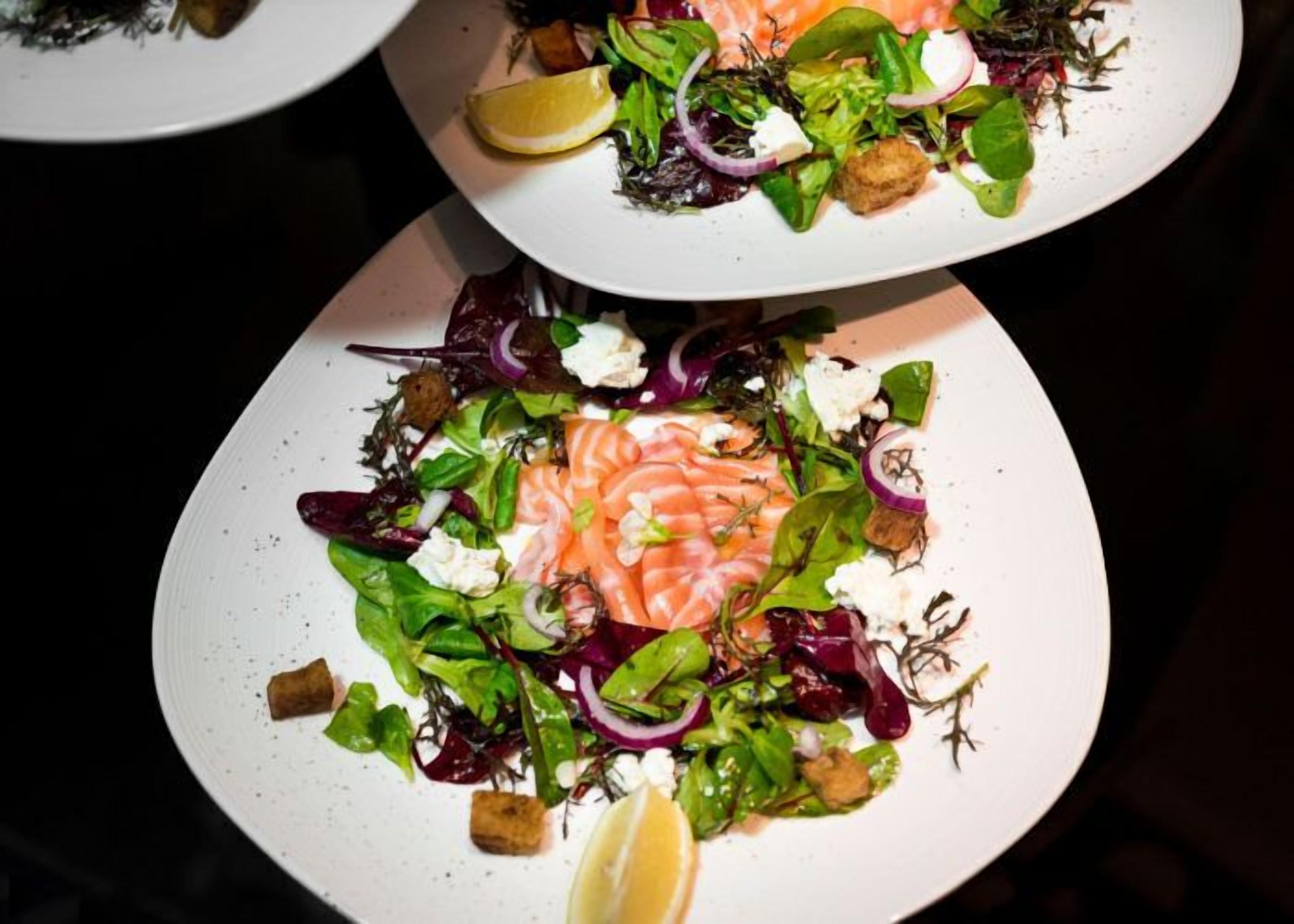 Prato de comida com salmão, folhas verdes e croutons.