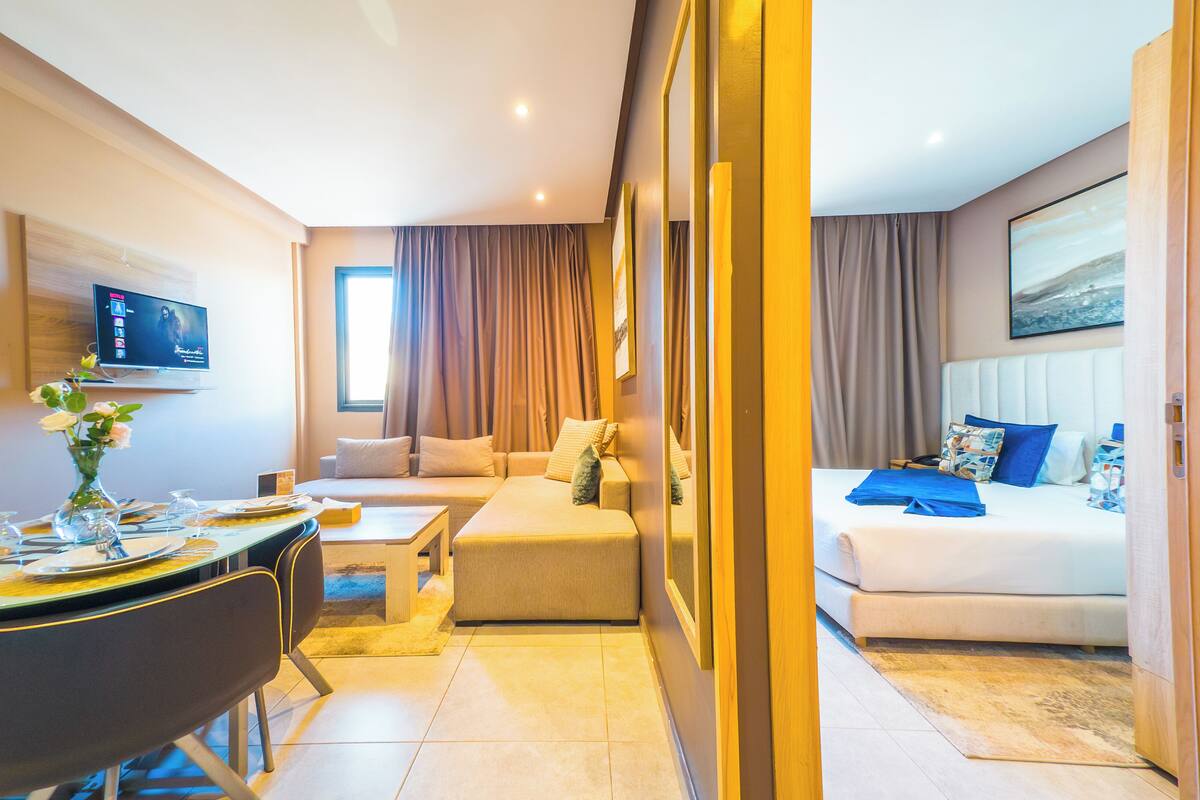 Quarto de hotel com área de jantar, sofá, cama e televisão.