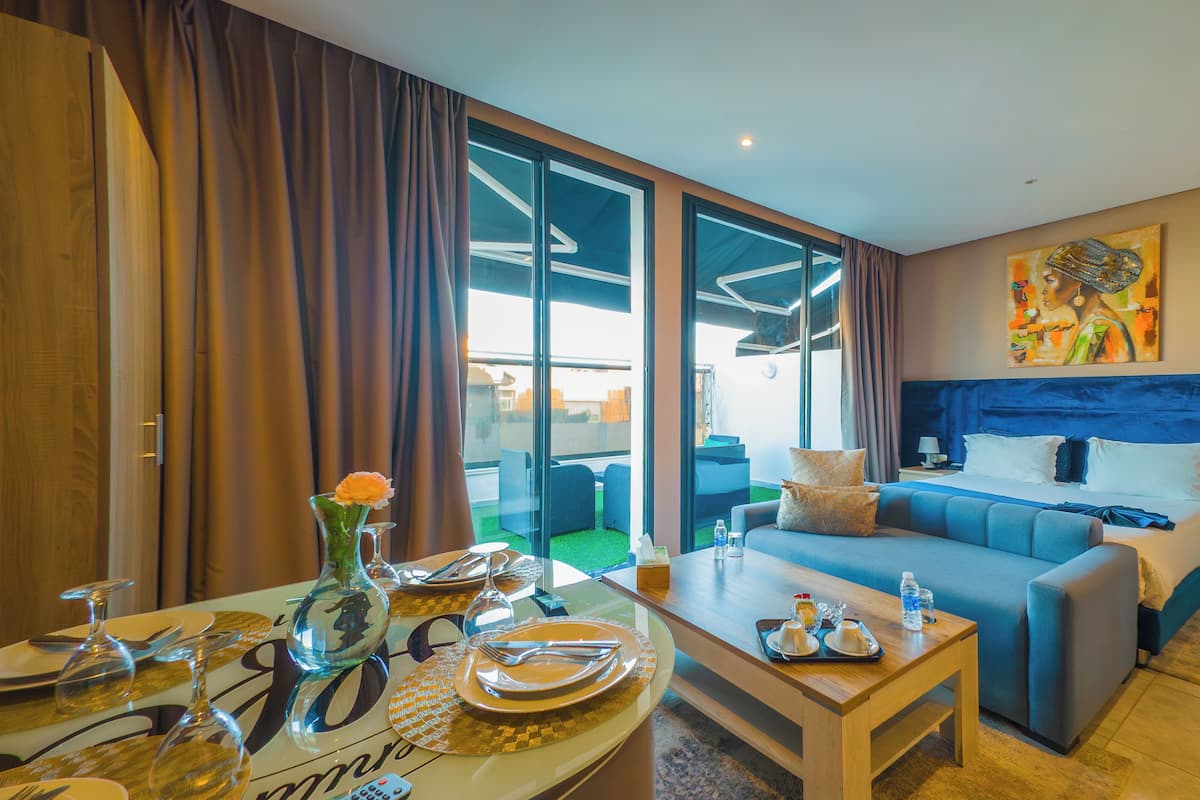 Quarto de hotel com cama, sofá, mesa de jantar posta com pratos e copos, e um quadro na parede.