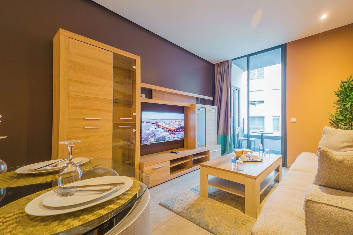 Uma sala de estar moderna com televisão, mobiliário de madeira, um espaço de refeições e uma janela grande.