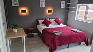 Quarto moderno com cama, mesas de cabeceira, uma pequena mesa com uma planta e luminárias fixadas na parede.