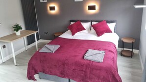 Quarto moderno com uma cama grande, duas mesas de cabeceira, escrivaninha e arte decorativa na parede.