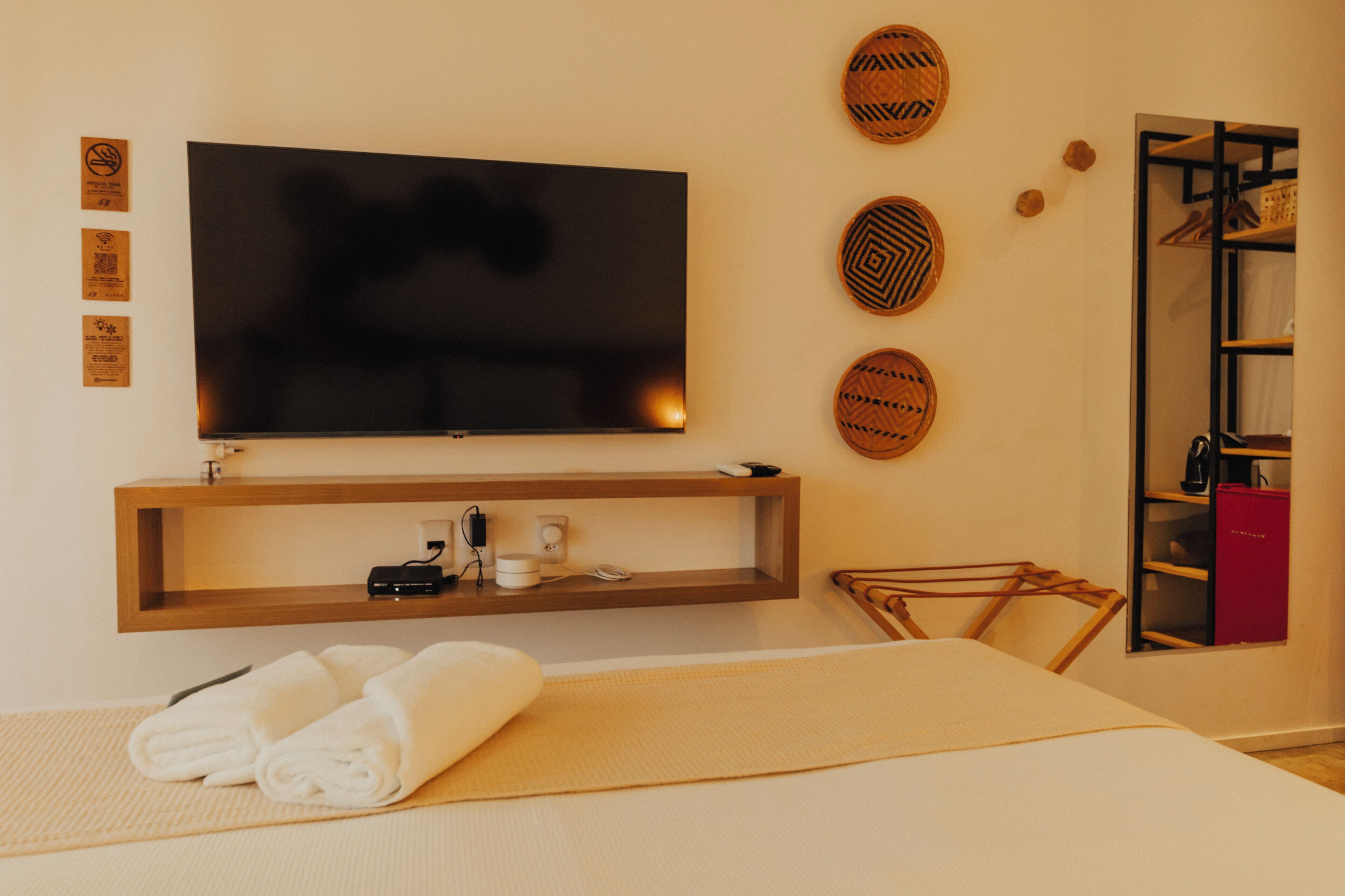 Quarto de hotel com cama, televisão, prateleira com produtos de higiene e guarda-roupa.