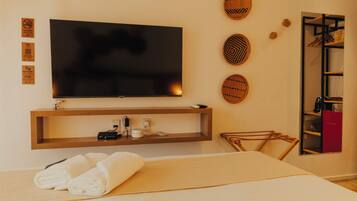 Quarto de hotel com cama, televisão, prateleira com produtos de higiene e guarda-roupa.