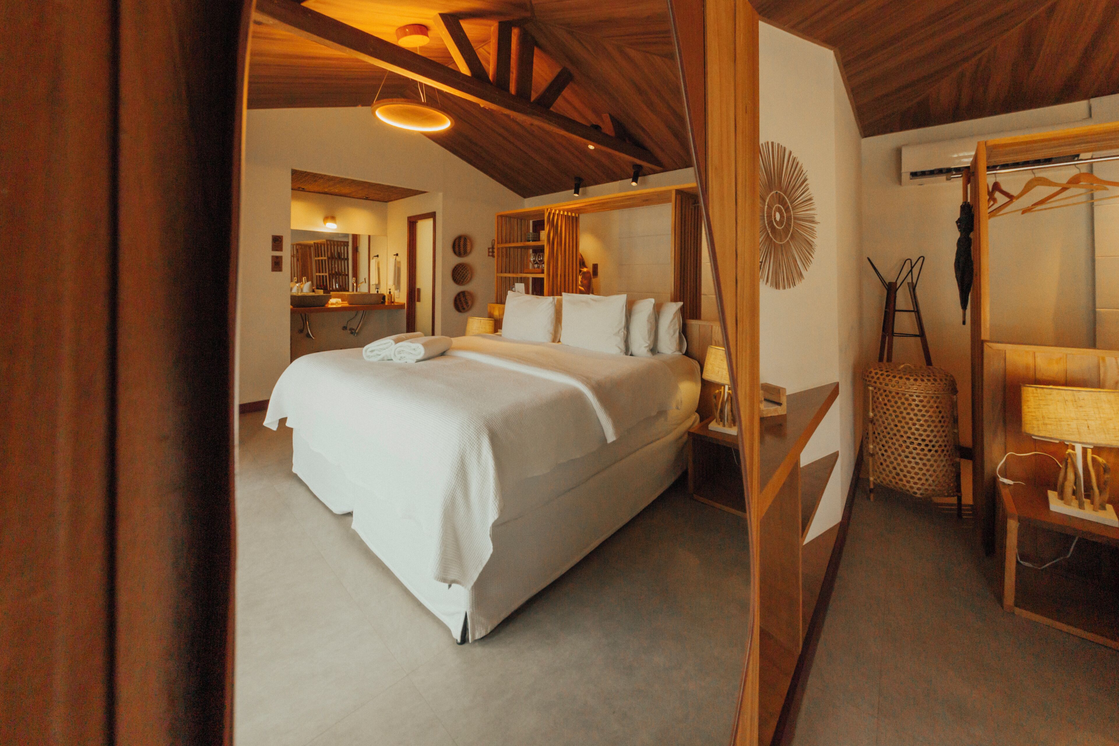 Quarto com uma cama grande, teto de madeira, espelho, guarda-roupa e mesa de cabeceira.